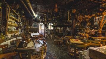 Um interior rústico com mobiliário de madeira, piso de pedra, utensílios de cozinha e diversos objetos decorativos.