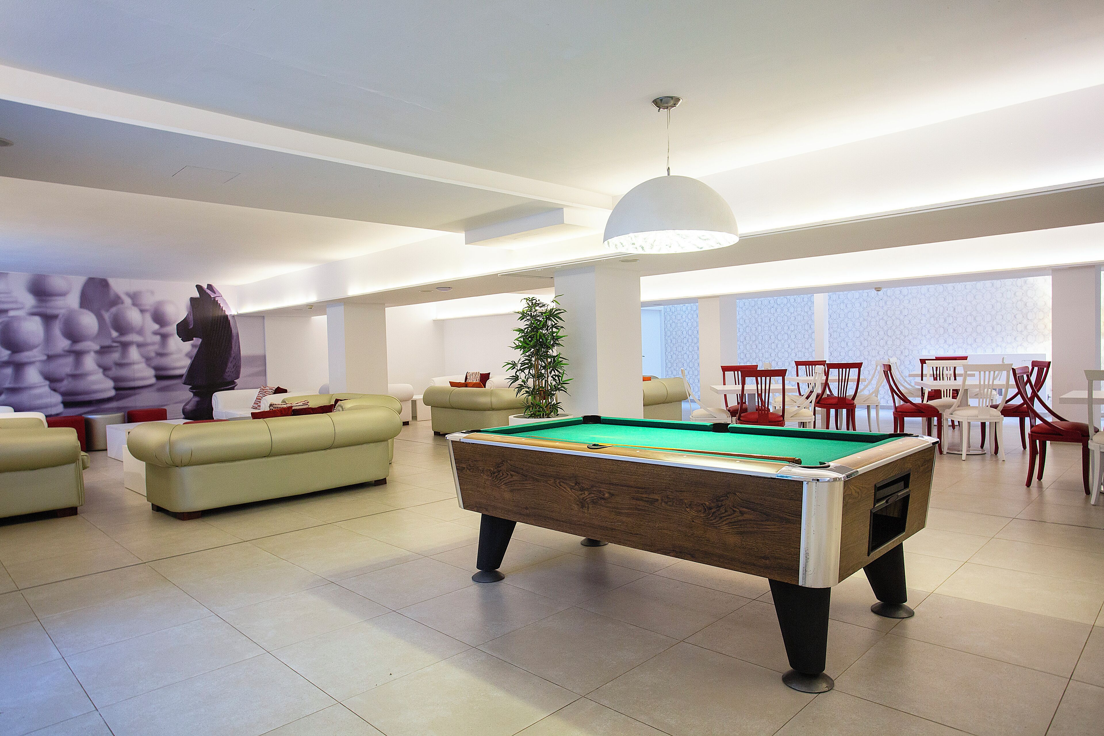 Uma sala de estar moderna com mesa de bilhar, sofás e um espaço de jantar com cadeiras vermelhas.