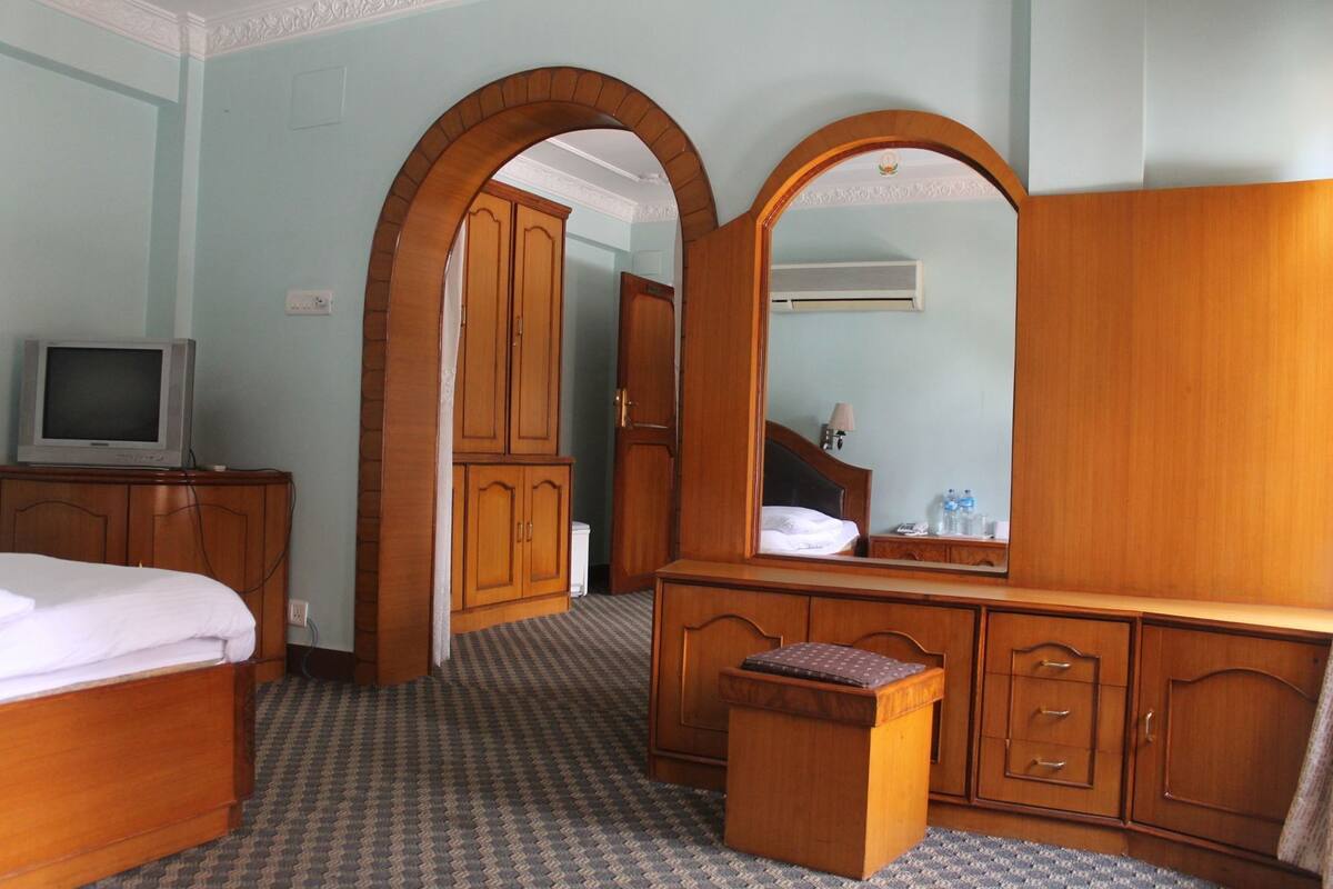 Quarto de hotel com cama, televisão, espelho grande e móveis de madeira.