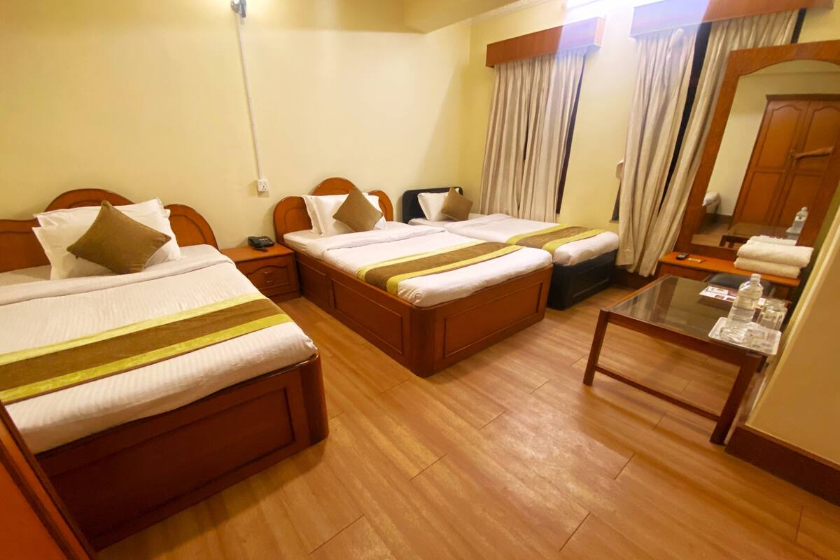 Quarto de hotel com duas camas, uma mesa pequena, um espelho e uma janela com cortinas.