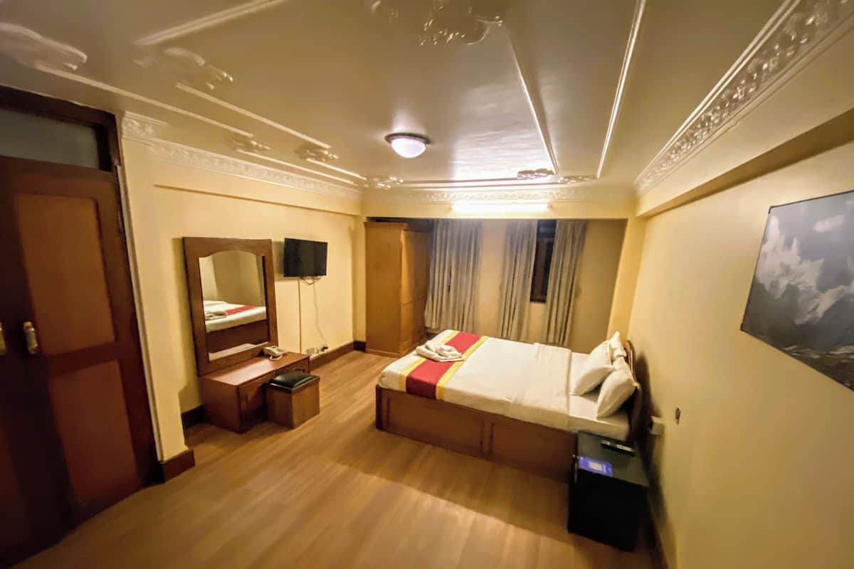 Quarto de hotel com cama, escrivaninha, espelho, televisão e guarda-roupa.