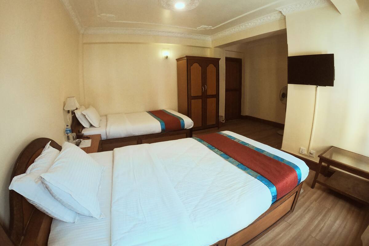 Quarto de hotel com duas camas, um guarda-roupa, uma televisão e uma escrivaninha.