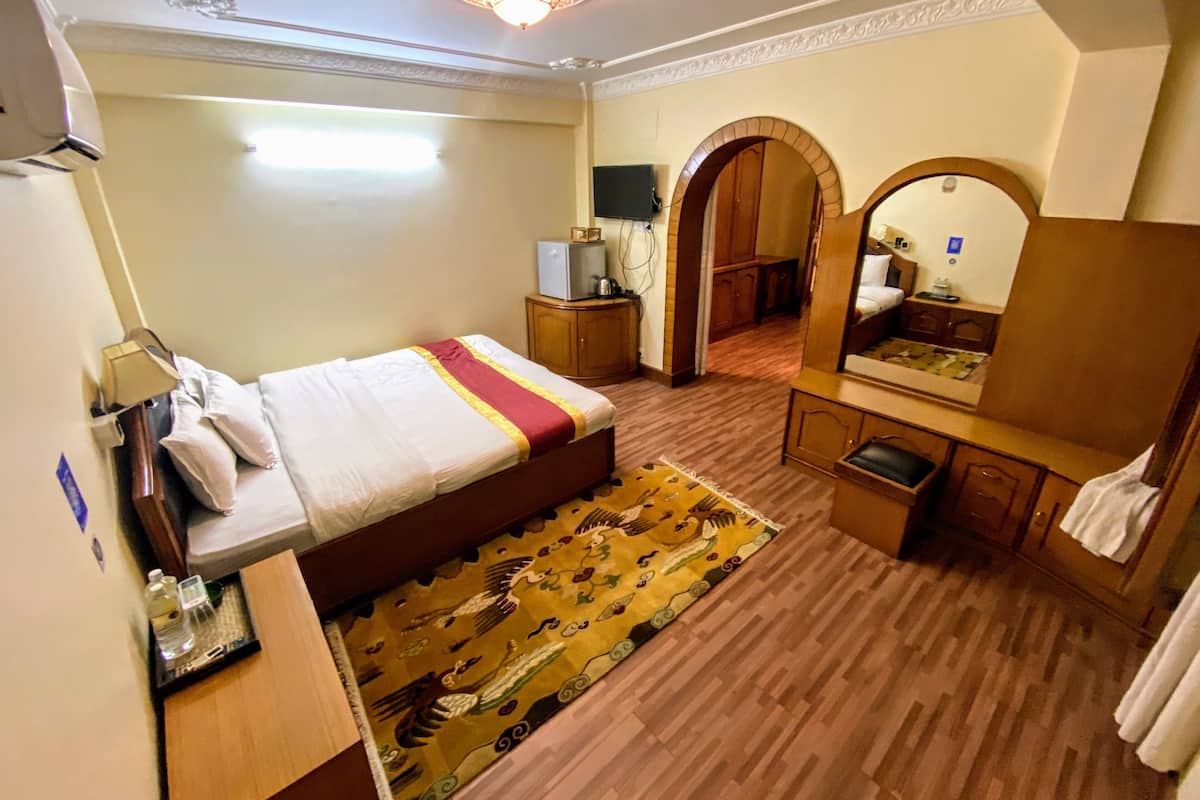 Quarto de hotel com cama, escrivaninha, espelho, guarda-roupa e banheiro com chuveiro e vaso sanitário.