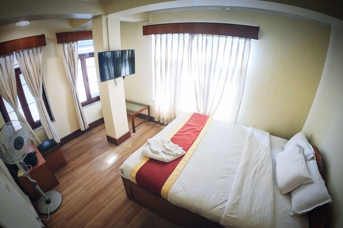 Quarto de hotel com cama, televisão, ventoinha e cortinas.