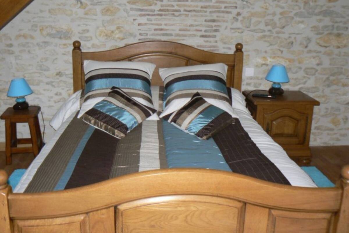 Uma cama de madeira com roupa de cama listrada, duas mesas de cabeceira com luminárias e uma parede de pedra.