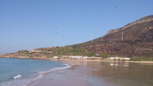 Uma praia com águas cristalinas, faixa de areia e um relevo acidentado ao fundo.