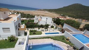 Área residencial com piscina, praia e uma colina ao fundo.