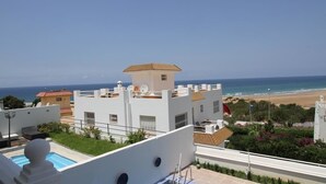 Um edifício branco com piscina no terraço e vista para a praia.