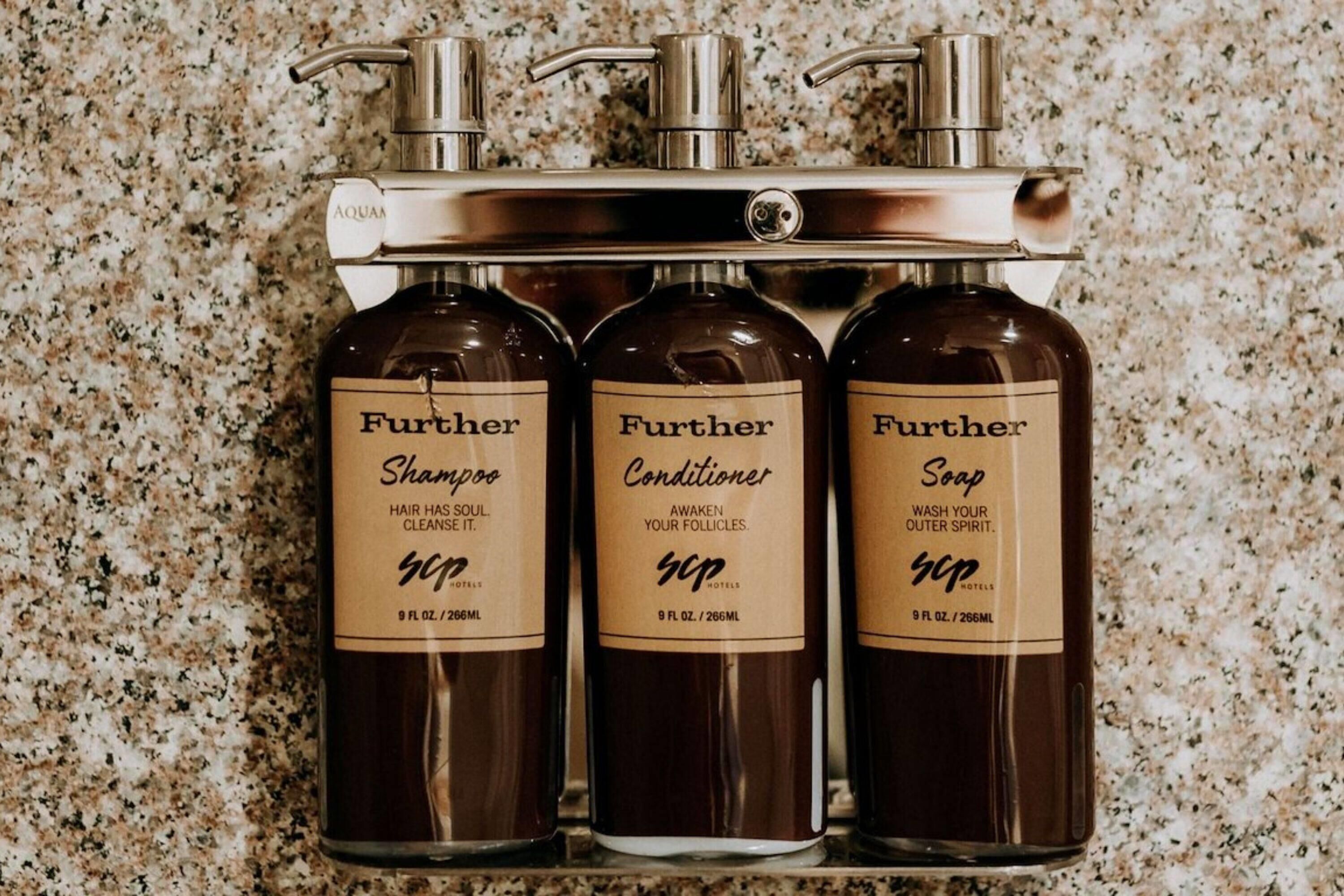 Três frascos de produtos Further para cabelo em um dosador metálico.