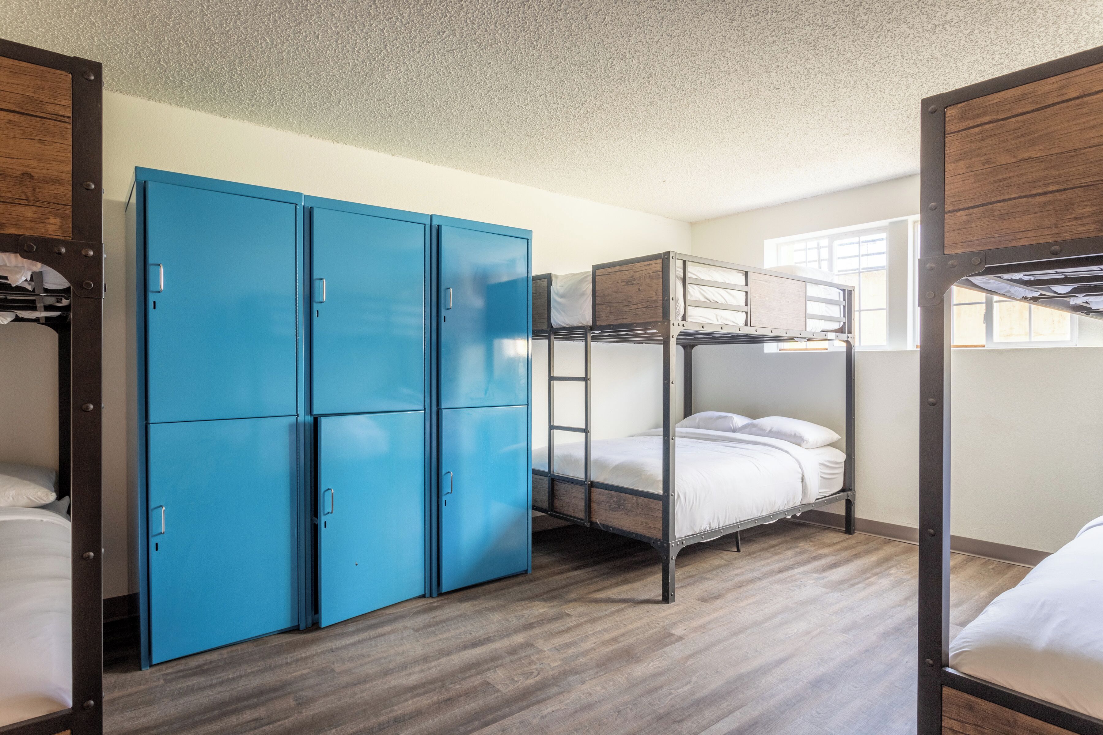 Uma cama beliche com cabeceira de madeira, um guarda-roupa azul e piso de madeira.