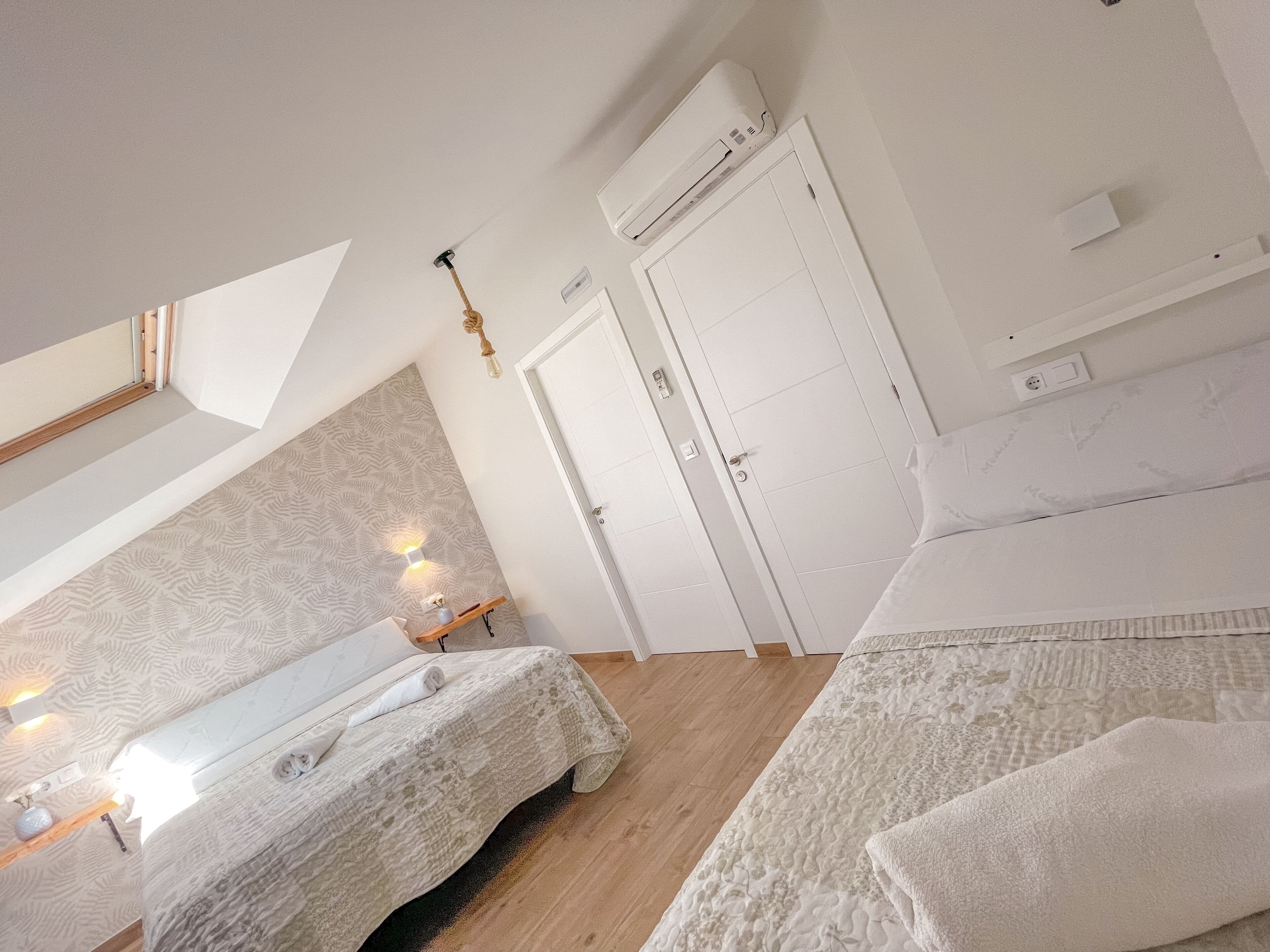 Quarto com duas camas, claraboia, aparelho de ar condicionado e parede com padrão.