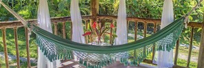Uma rede pendurada entre vigas de madeira em um ambiente externo exuberante e verdejante.