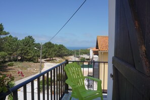 Uma varanda com uma cadeira verde, vista para o mar e um edifício com telhado de azulejos.