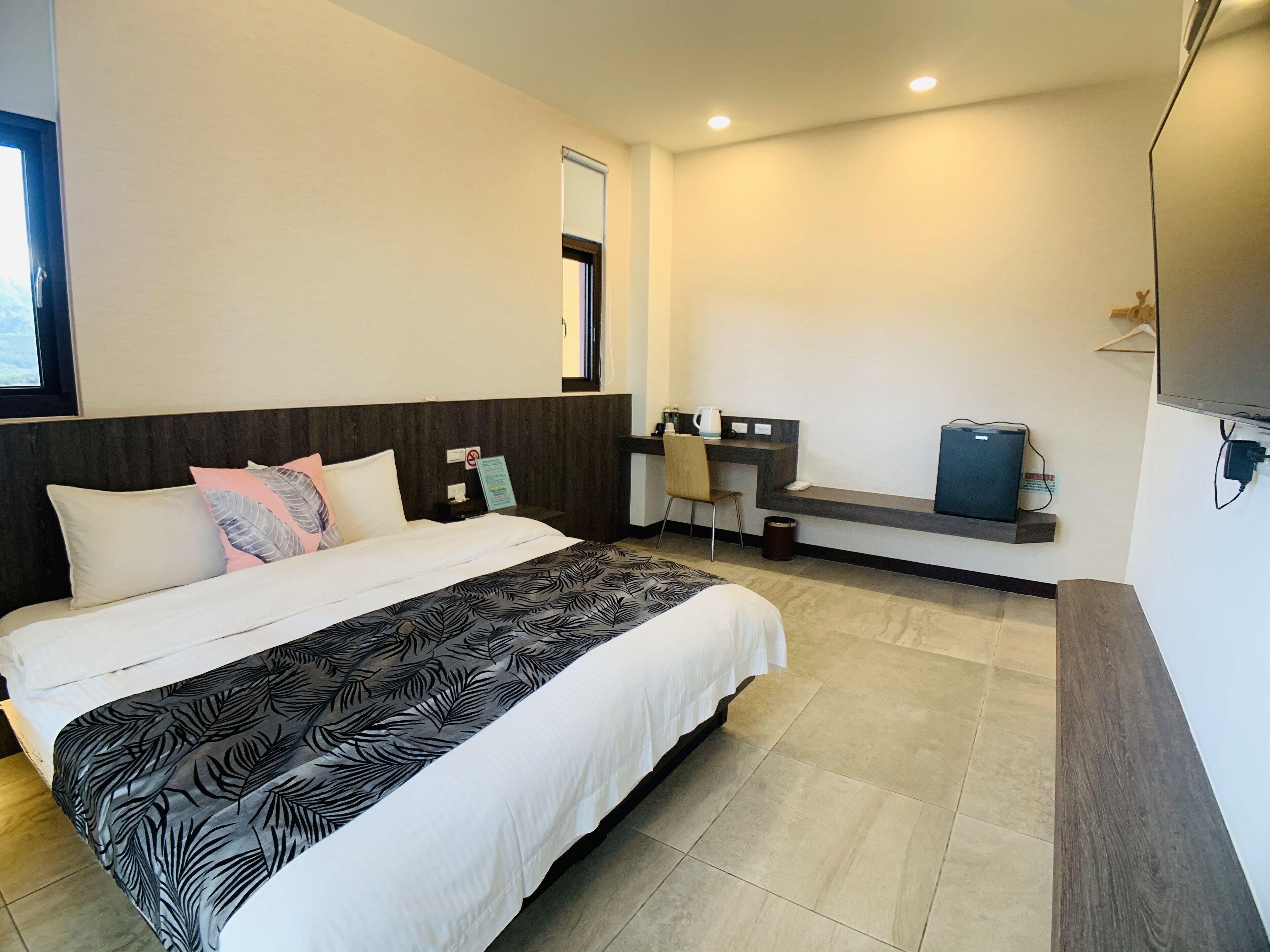 Quarto de hotel moderno com uma cama grande, uma escrivaninha, uma cadeira e uma televisão.