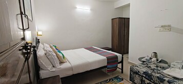 Uma cama de solteiro com manta listrada, uma pequena mesa de cabeceira com chaleira, um armário e um luminário fixado na parede.