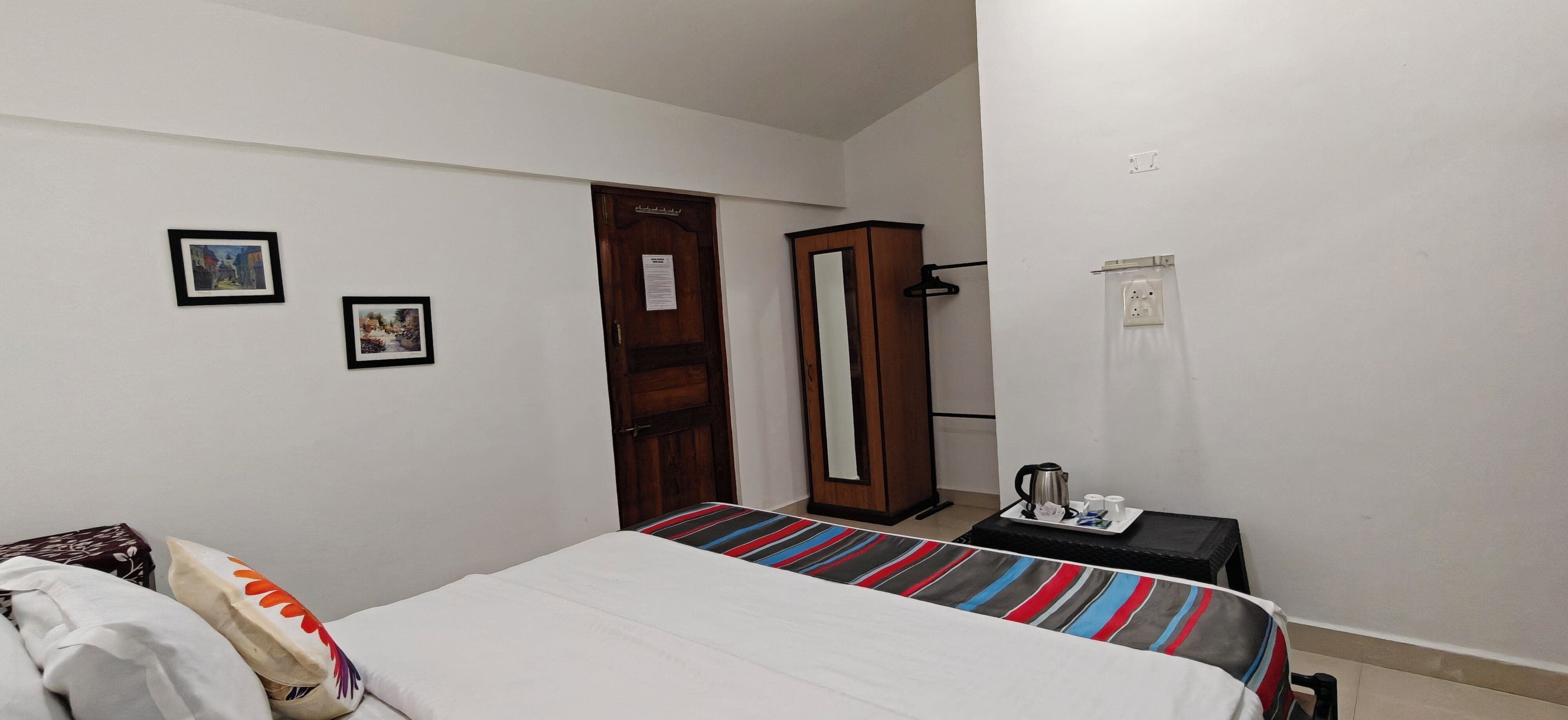 Quarto com cama, guarda-roupa, espelho e uma pequena mesa com chaleira e chávenas.