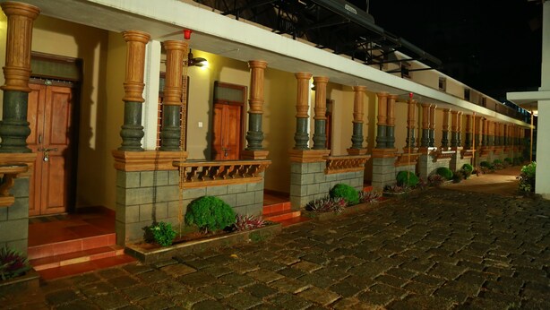 Um edifício com várias portas de madeira, colunas, entrada em pedra e uma escadaria que leva ao segundo andar.