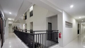 Corredor moderno e bem iluminado, com corrimão de metal preto, um extintor de incêndio e chão de azulejos brancos e impecáveis.