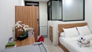 Quarto de hotel moderno com uma cama de madeira, uma pequena escrivaninha com cadeira, um espelho e um ar condicionado.