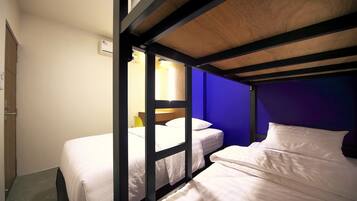 Quarto com beliches, teto de madeira e parede azul. Há uma janela com luz natural.
