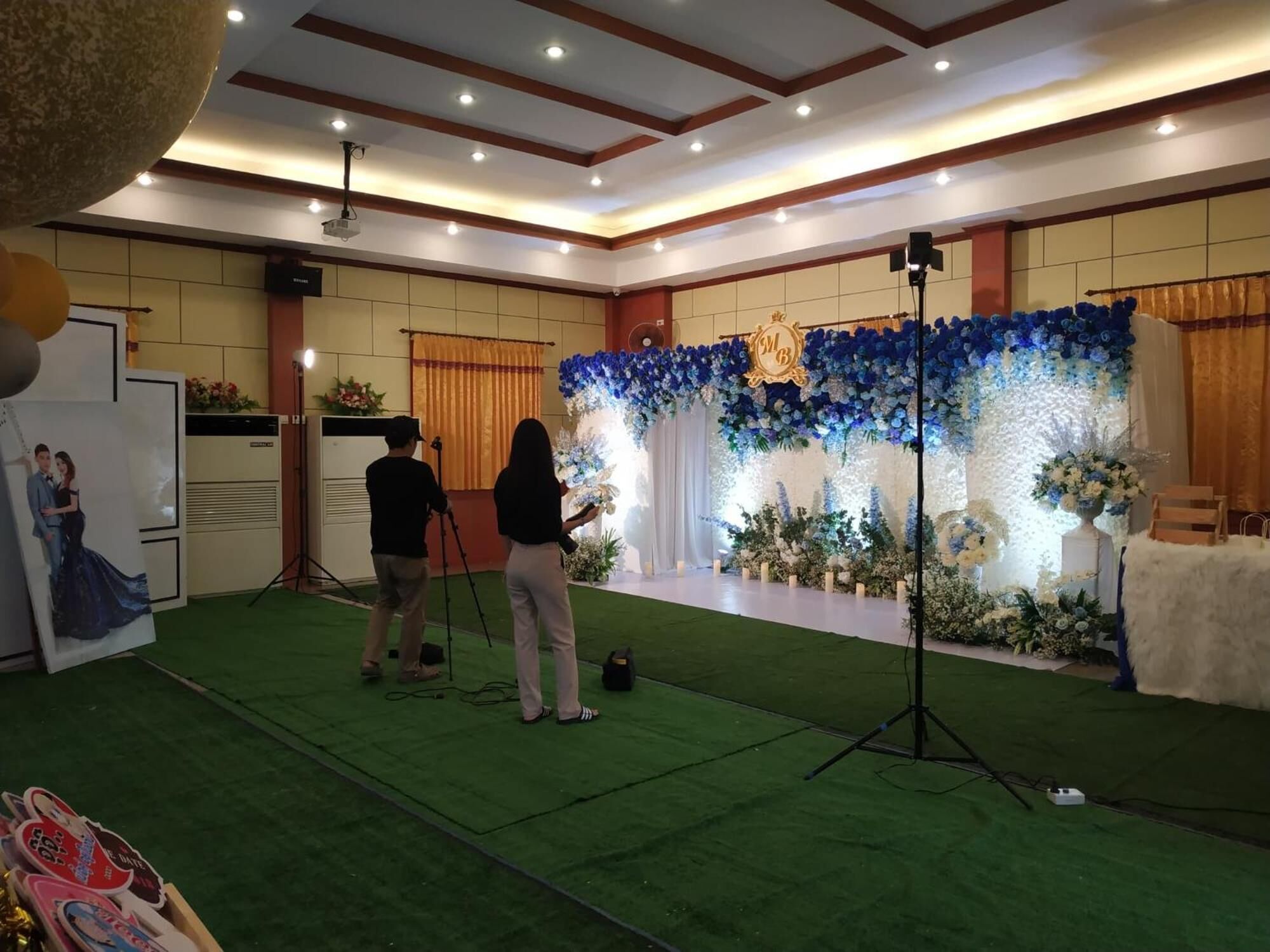 Um palco com um painel de fundo de flores azuis e brancas, um suporte de microfone e uma câmera sobre um tripé.
