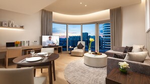 Uma sala de estar moderna com área de jantar, televisão e uma grande janela com vista para a cidade.