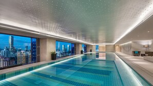Piscina interior moderna com vista para a cidade, um corredor longo e uma área de estar também com vista.