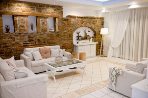 Sala de estar com móveis brancos, parede de pedra e um espelho decorativo.