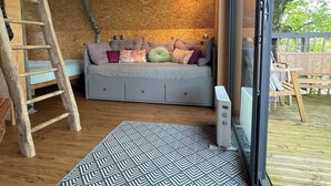 Um quarto aconchegante com teto inclinado, um sofá cinza com almofadas, uma escada de madeira e um tapete estampado.