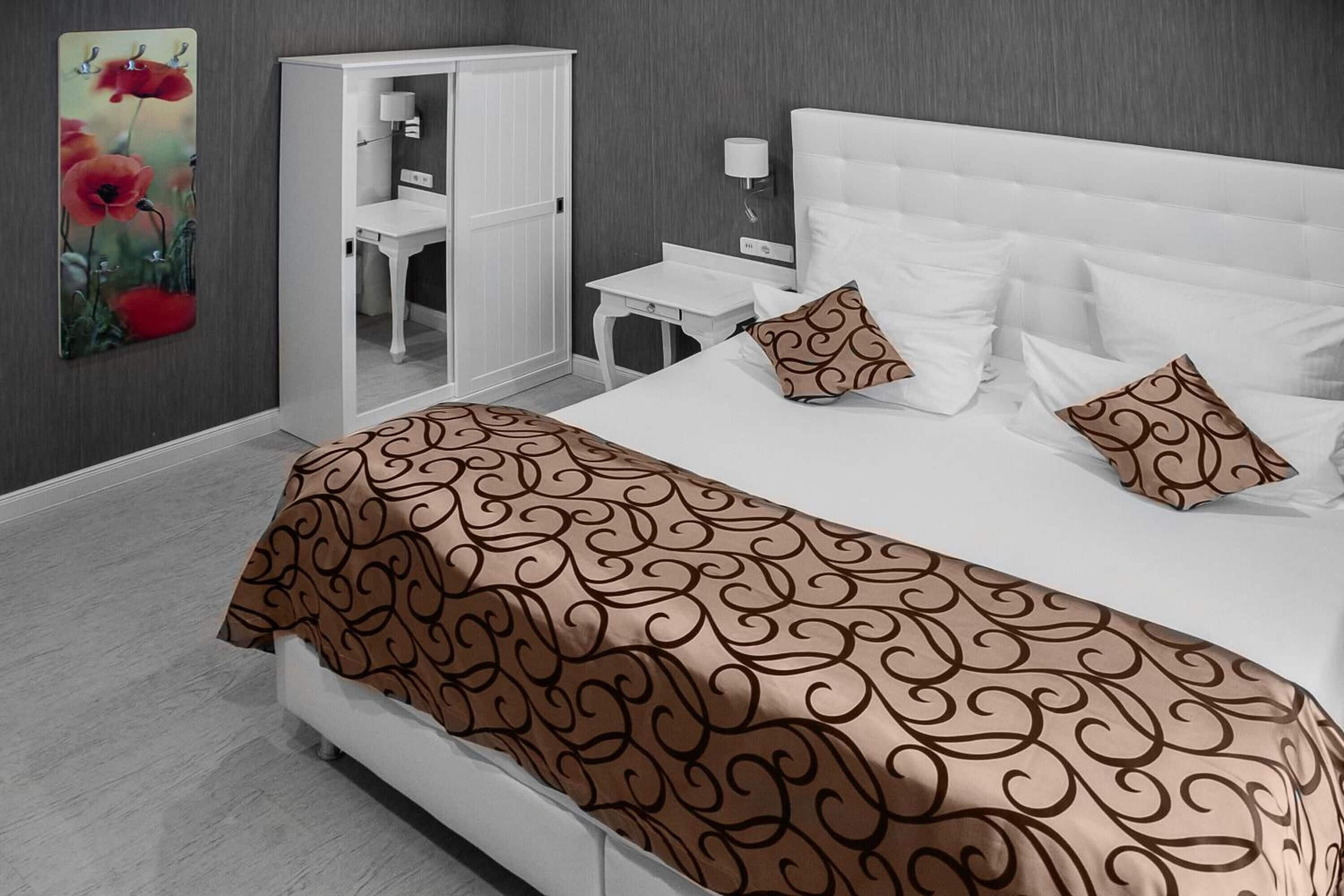 Quarto moderno com uma cama grande, cabeceira branca e manta decorativa estampada.