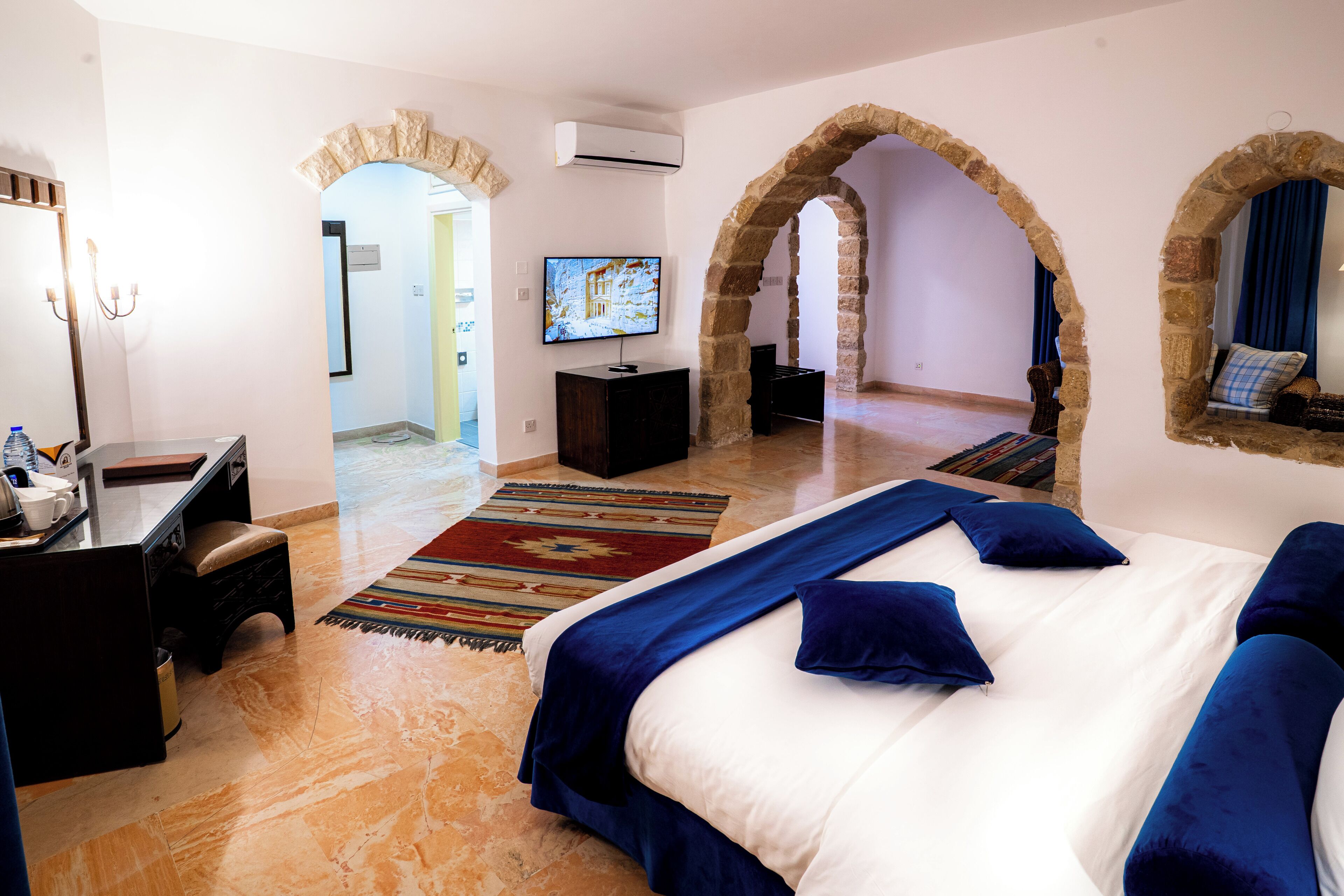 Quarto de hotel com uma cama grande, uma escrivaninha com computador, televisão e arcos de pedra.
