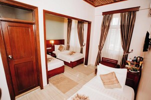 Quarto de hotel com duas camas, porta de madeira, espelho, mesa de cabeceira e escrivaninha com luminária.