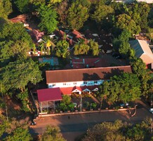 Vista aérea de uma área residencial com várias casas, um edifício grande com telhado vermelho e vegetação ao redor.