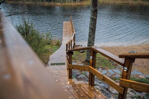 Um calçadão de madeira que leva a um lago, com uma grade de madeira e uma árvore por perto.