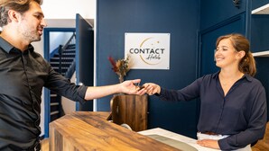 Balcão de recepção com bancada de madeira e uma placa com a inscrição 'CONTACT Hotels'.