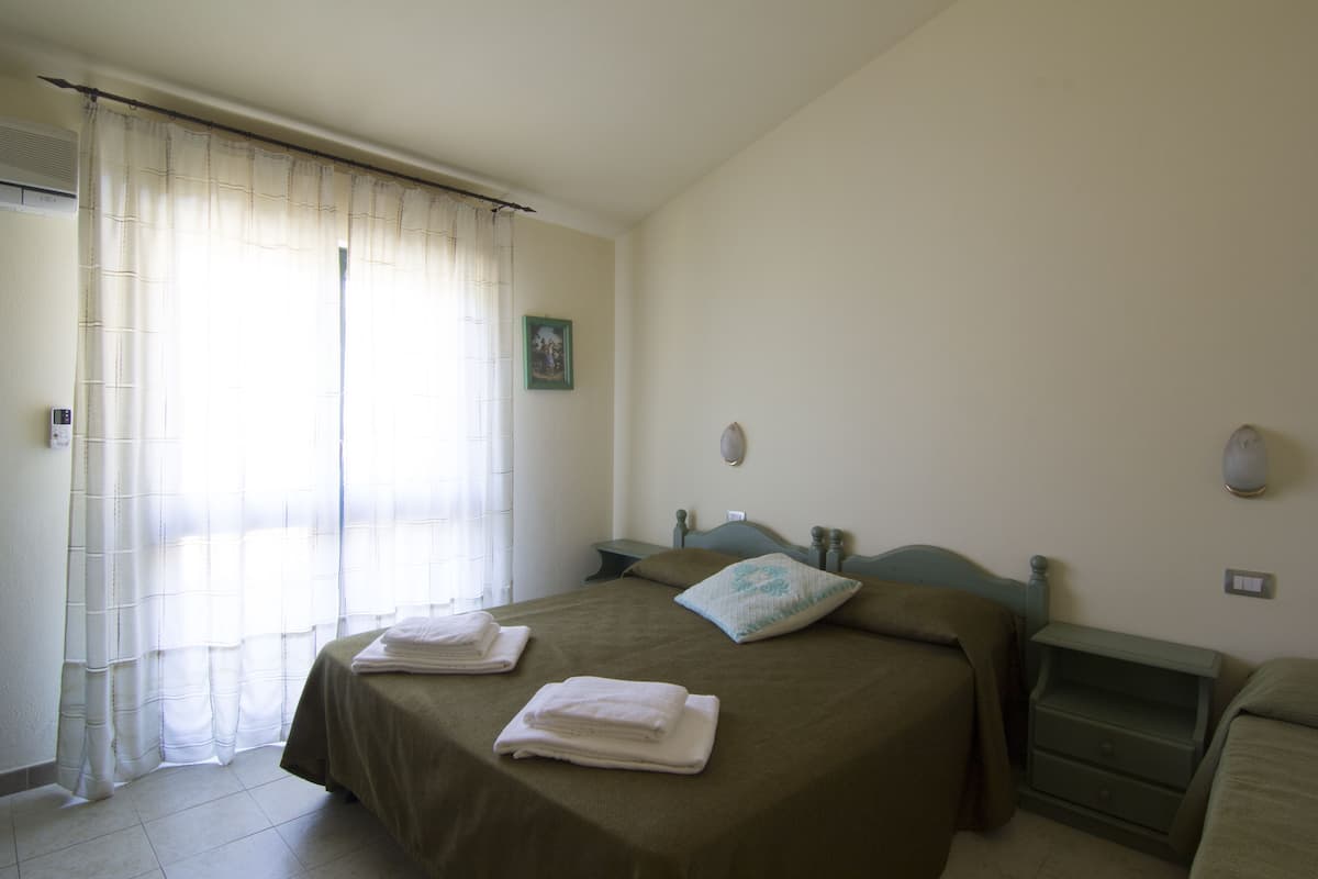 Quarto com duas camas, mesa de cabeceira e janela com cortinas.