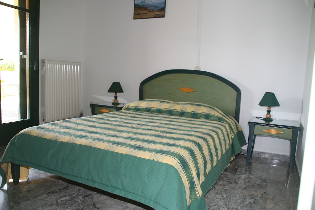 Quarto com uma cama, duas mesas de cabeceira, um radiador e um quadro na parede.