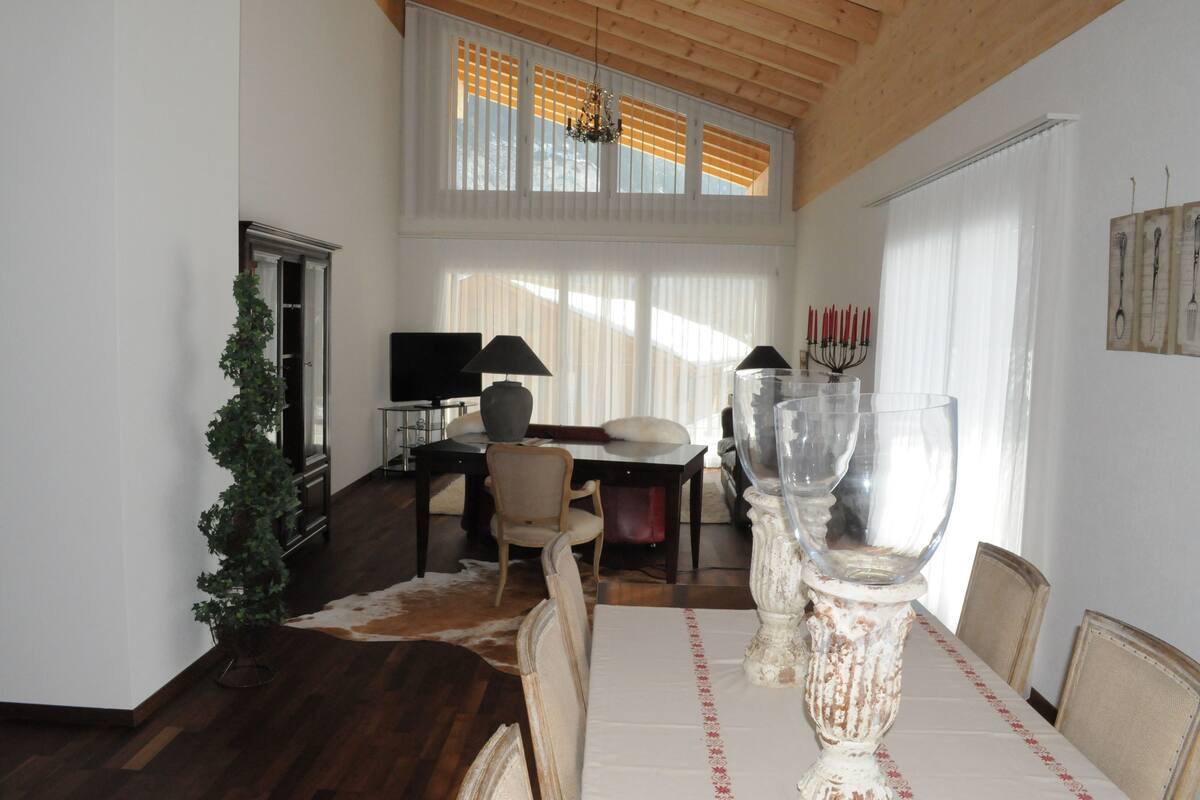 Uma sala de jantar com uma mesa posta para dois, um candelabro e uma menora no parapeito da janela.