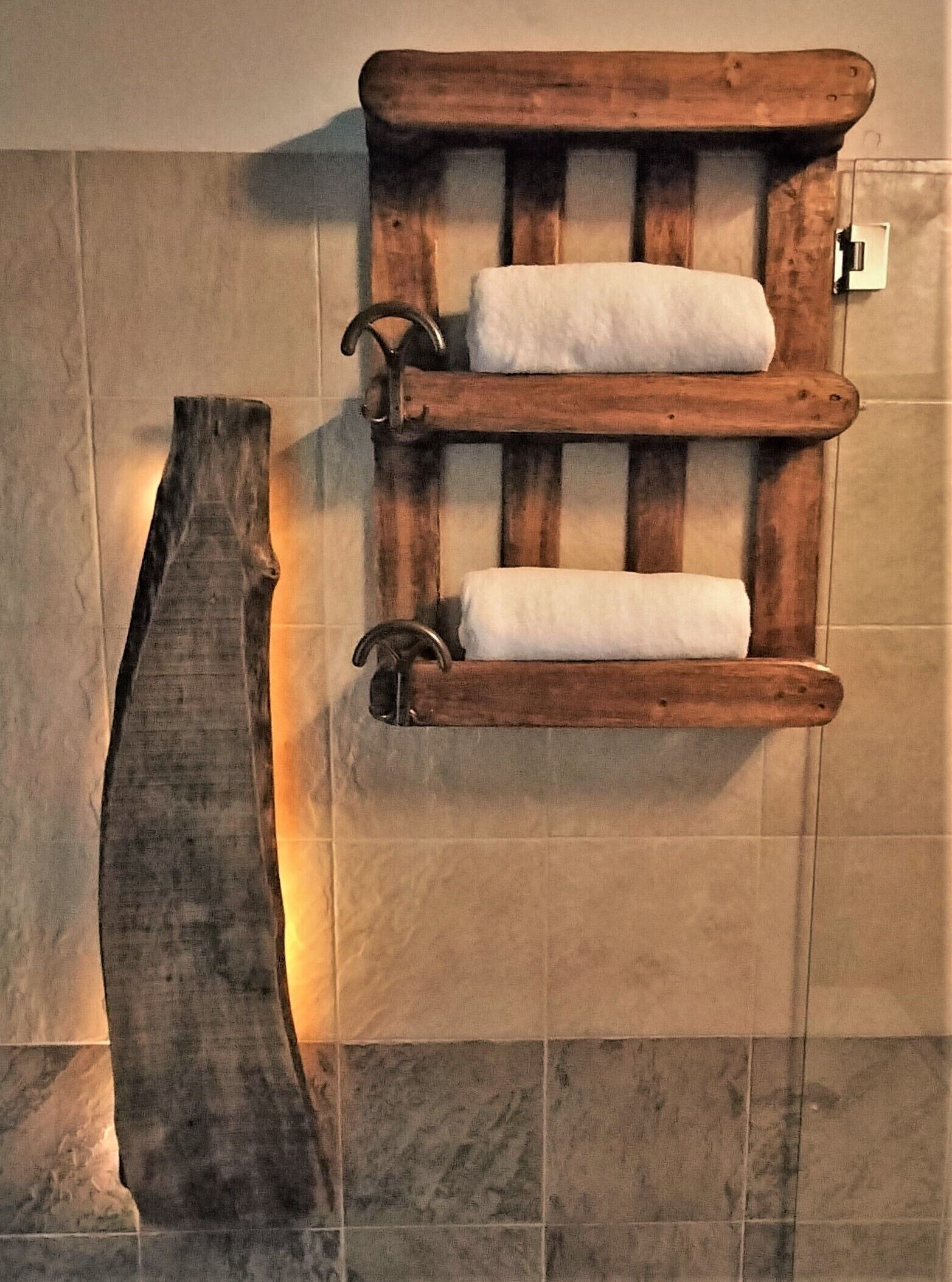 Um porta-toalhas de madeira com duas toalhas penduradas, fixado em uma parede revestida de azulejos.
