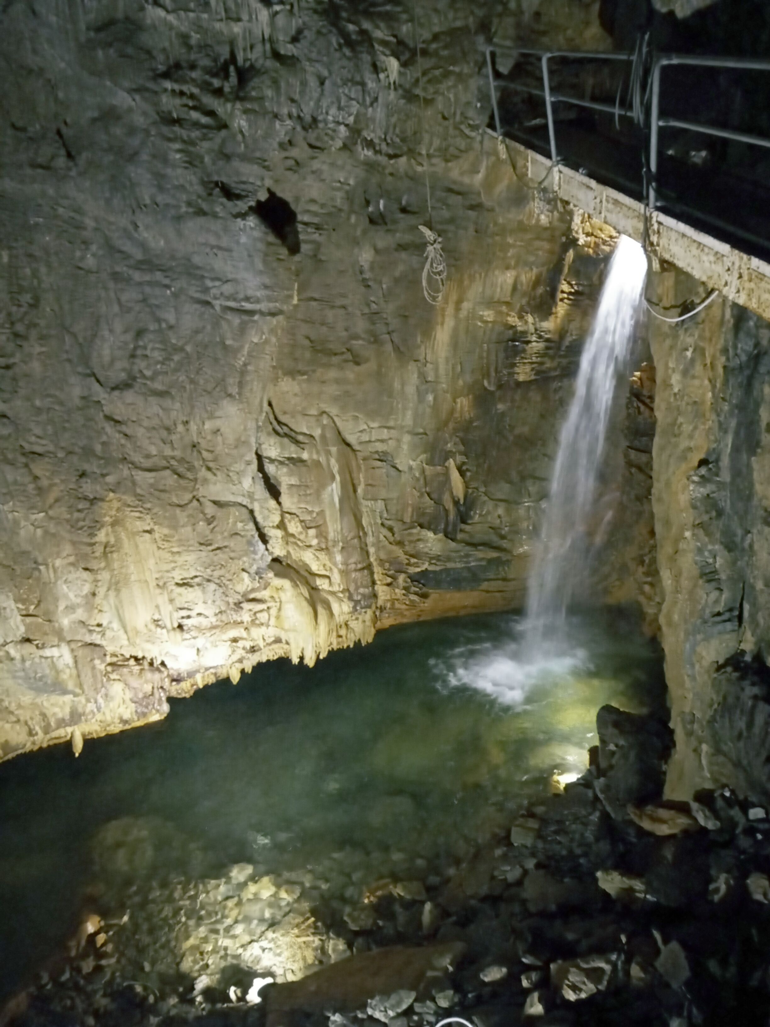 Caverna com uma cascata, paredes rochosas e um corrimão de metal.