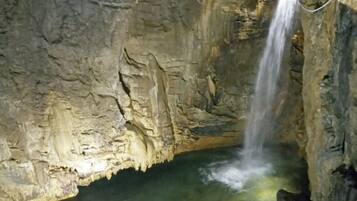 Caverna com uma cascata, paredes rochosas e um corrimão de metal.