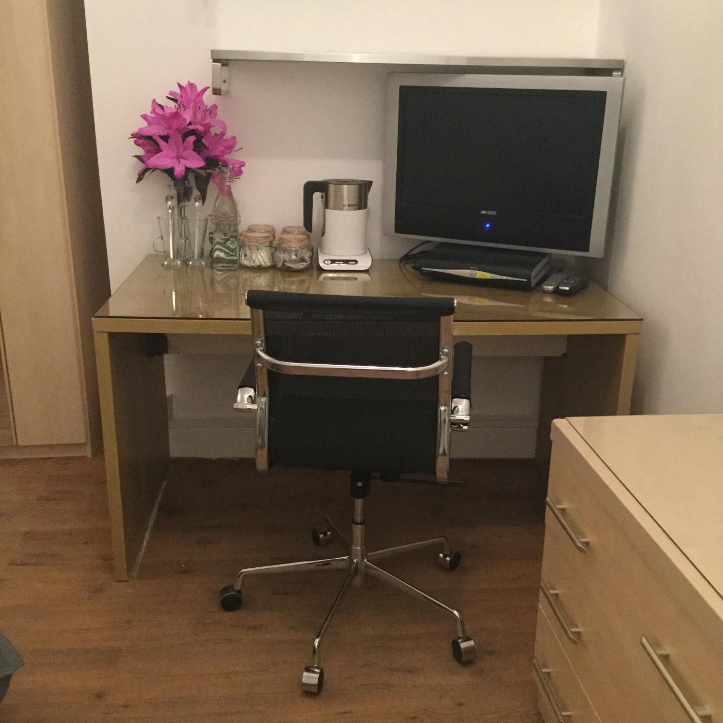 Um espaço de trabalho compacto com escrivaninha, laptop, cafeteira, cadeira e cómoda.