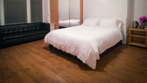 Quarto com cama, sofá preto, guarda-roupa de madeira e mesa de cabeceira com um vaso de flores.