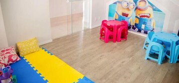 Espaço infantil com uma cama pequena, tapete de brincadeira colorido e decoração de parede com tema Minion.