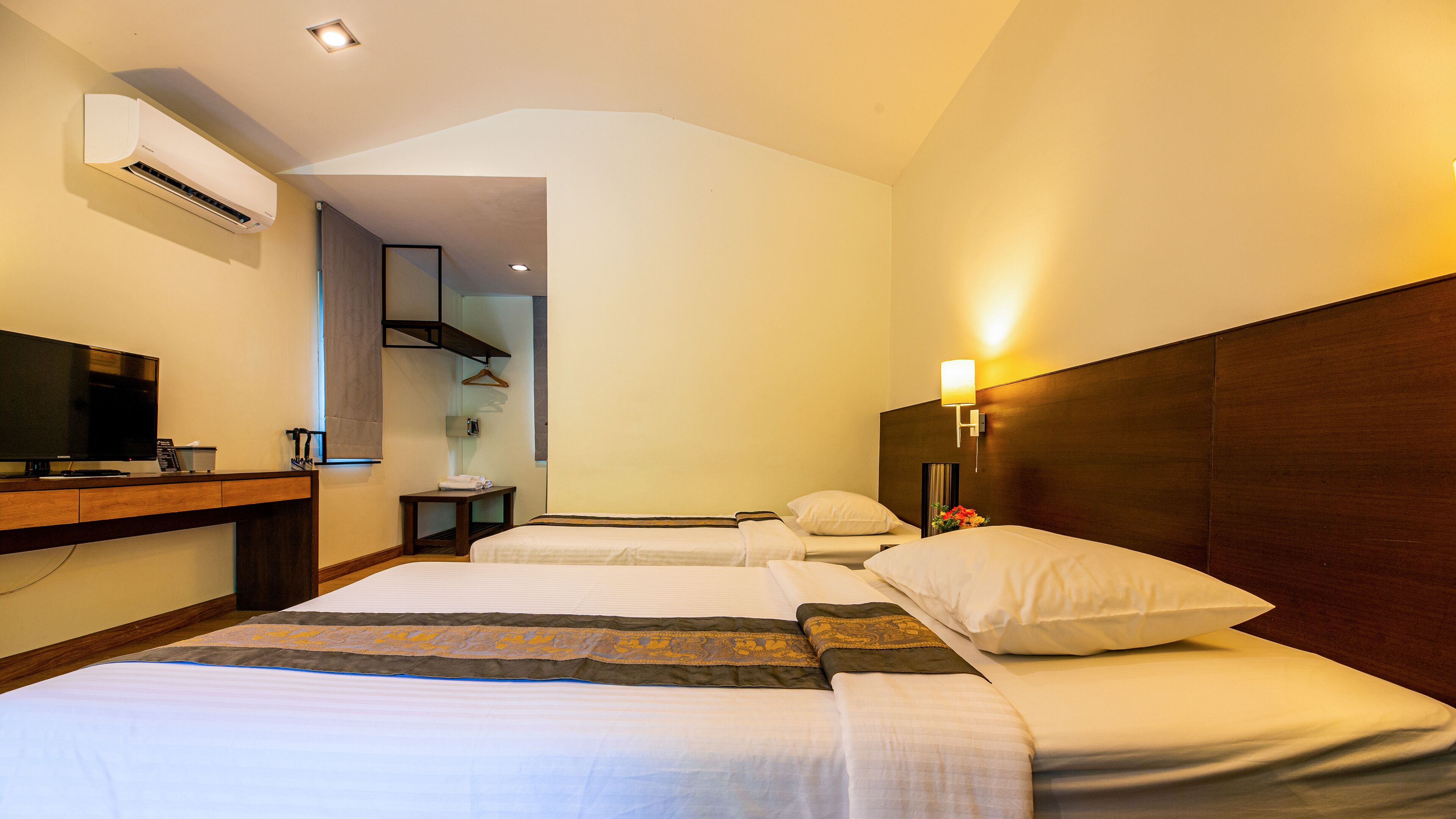 Quarto de hotel com duas camas, televisão, secretária e ar condicionado.