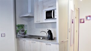 Uma cozinha moderna com armários brancos, uma pia de aço inoxidável, um micro-ondas e uma chaleira.