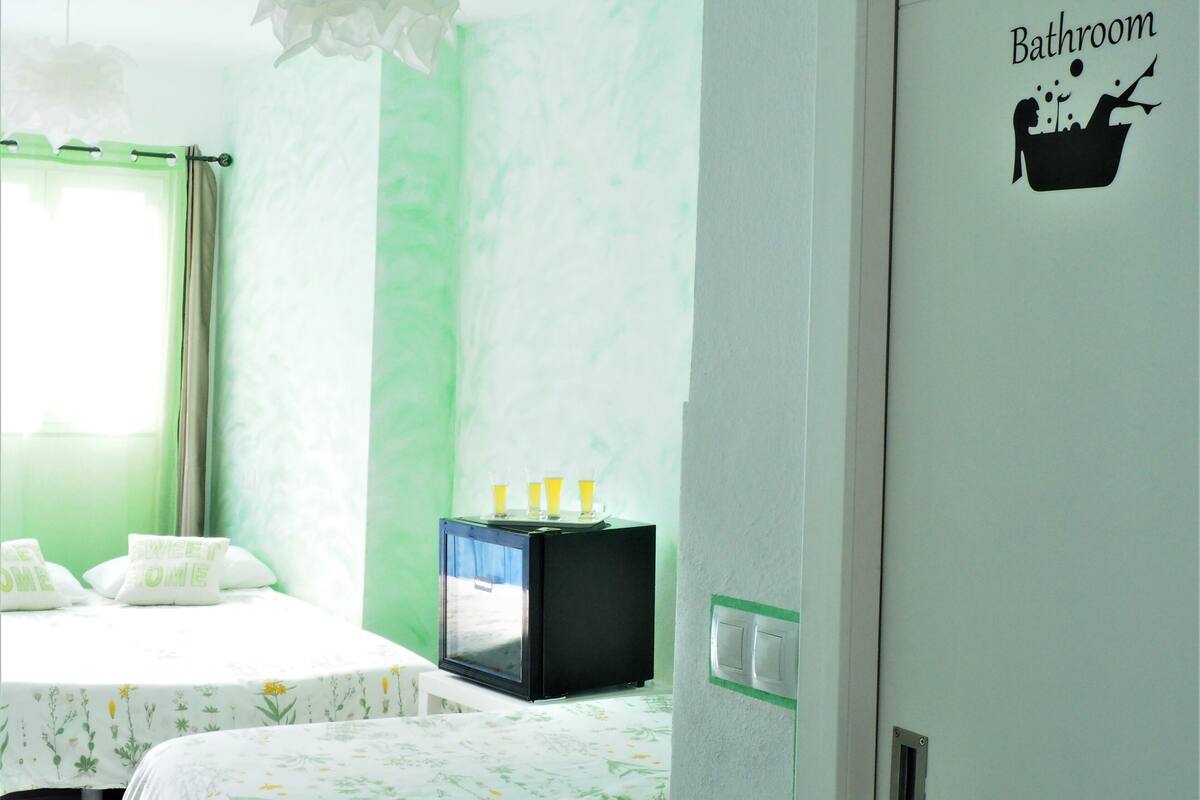 Quarto com duas camas, uma TV pequena e o símbolo de banheiro.