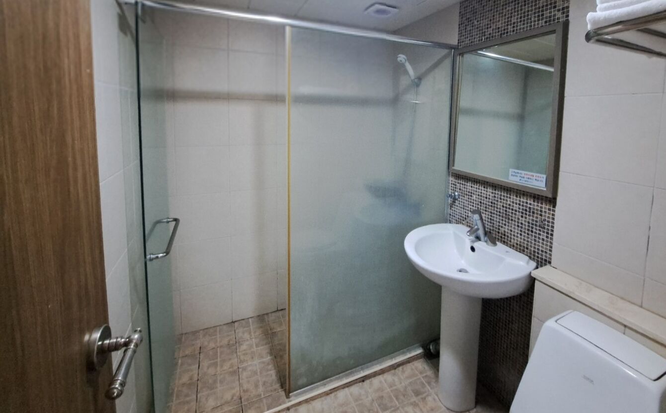 Casa de banho com chuveiro envolto em vidro, pia e sanita.