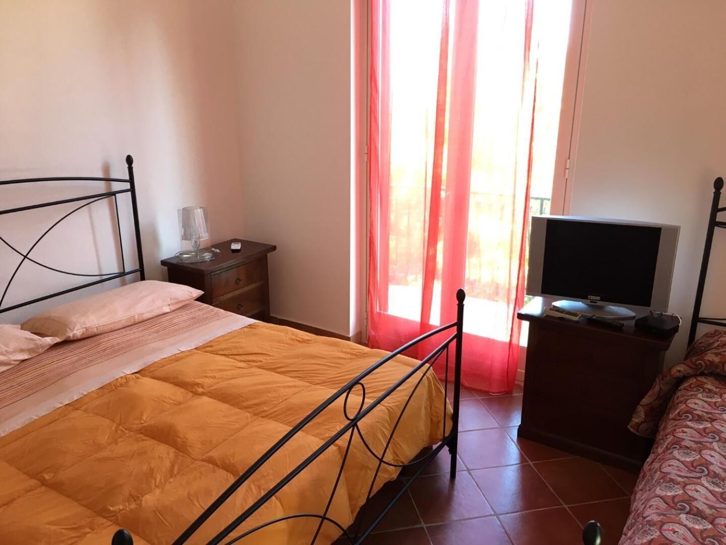 Quarto com cama, mesa de cabeceira, televisão e janela com cortinas.