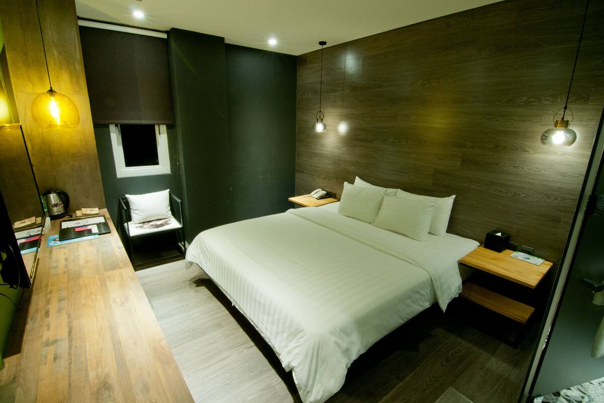 Quarto moderno com cabeceira de madeira, uma cama grande, mesas de cabeceira e uma escrivaninha com cadeira.
